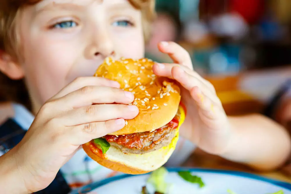 Dziecko zjada hamburger.